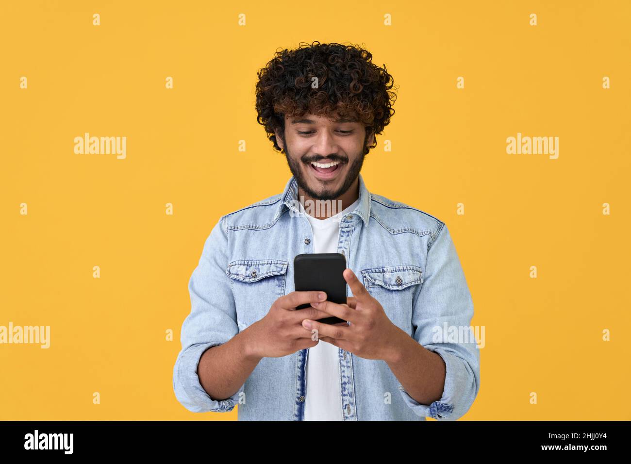 Happy indian young man using cell phone isolated on yellow background ...