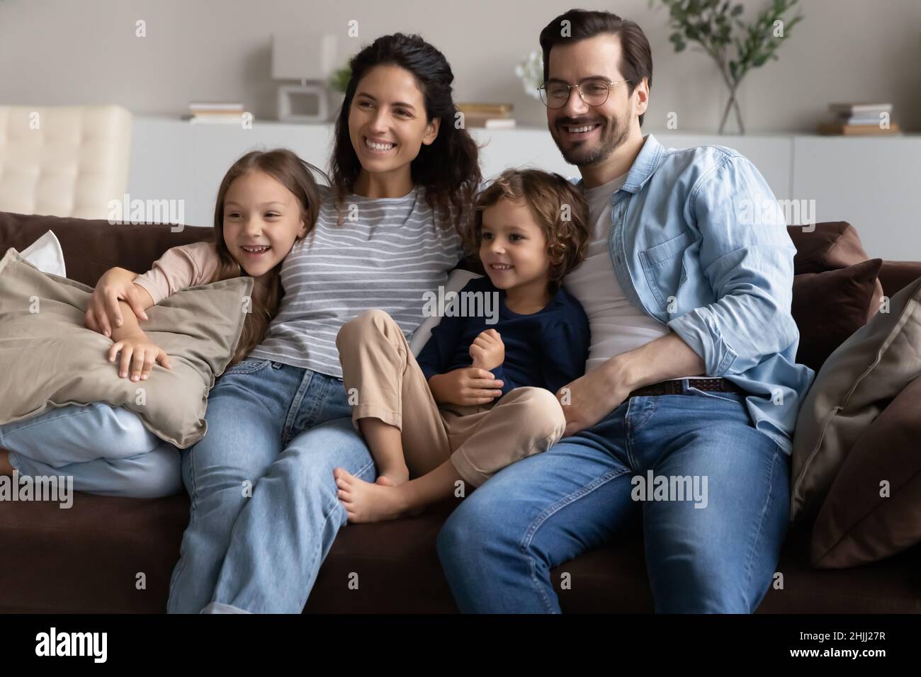 Family sitting on sofa at home smiling looking into distance Stock ...