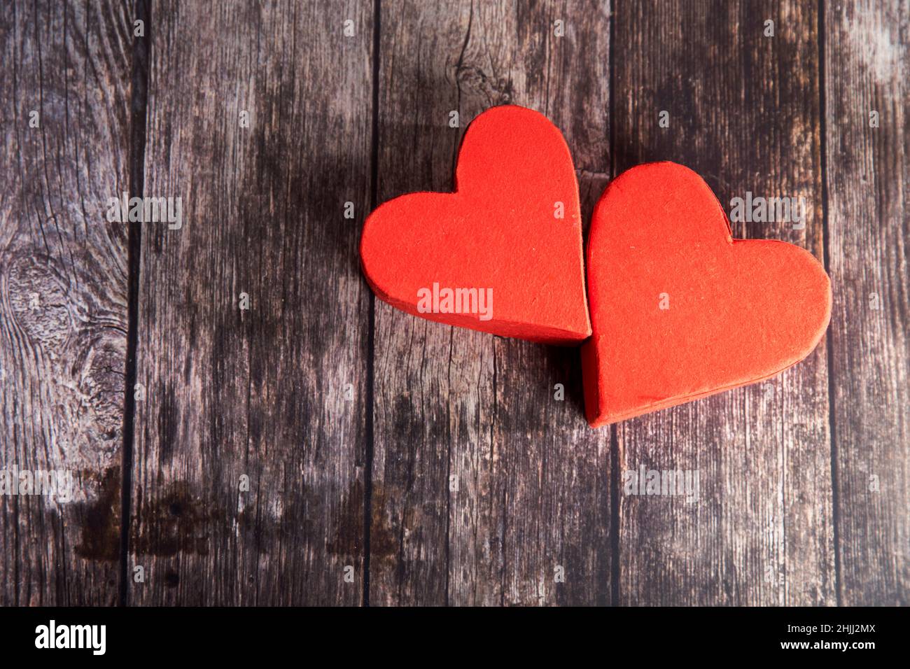 Two red paper hearts are next to each other on a wooden brown table ...