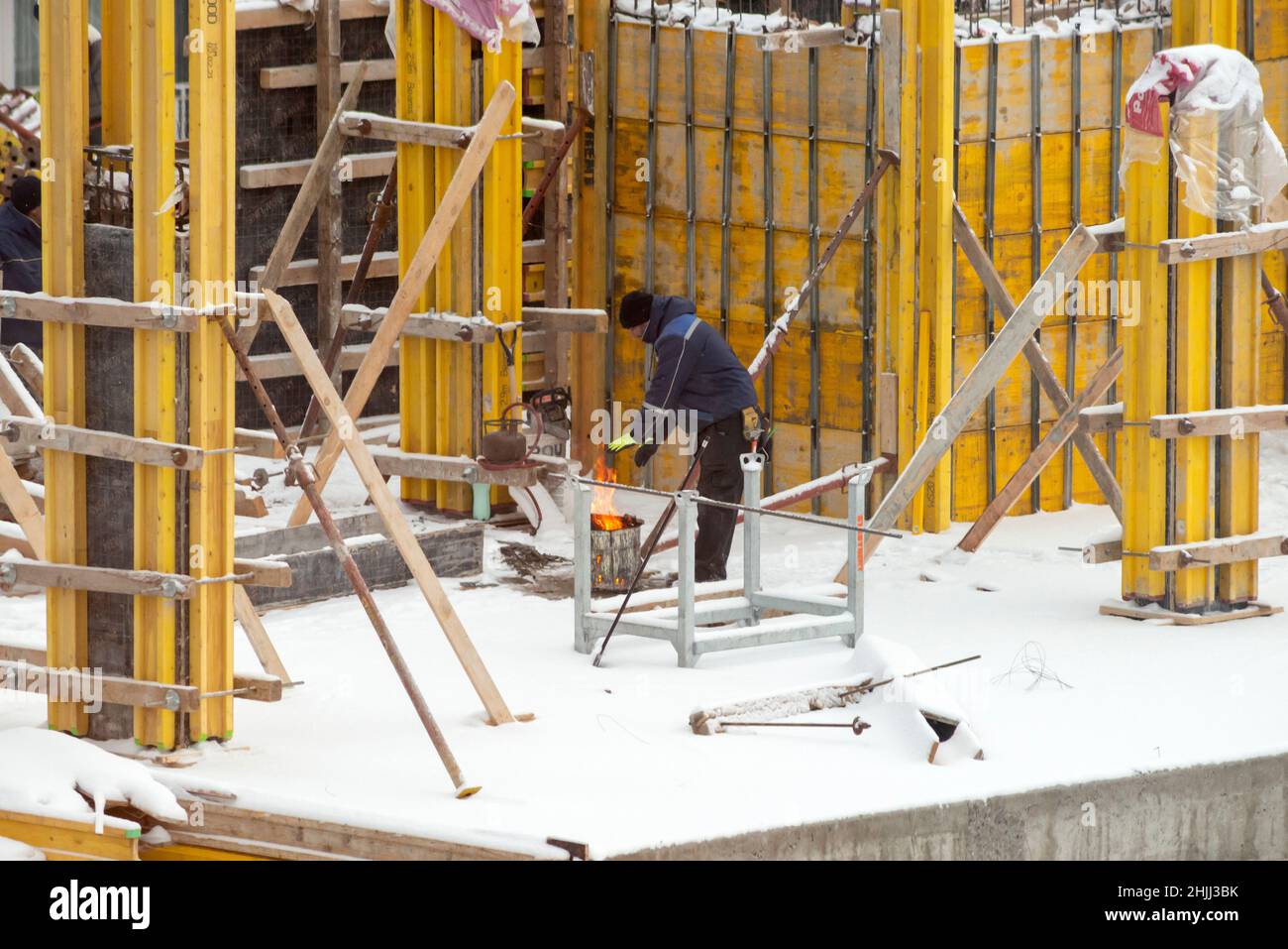 Worker using fire in a bucket to warm himself up during building works ...