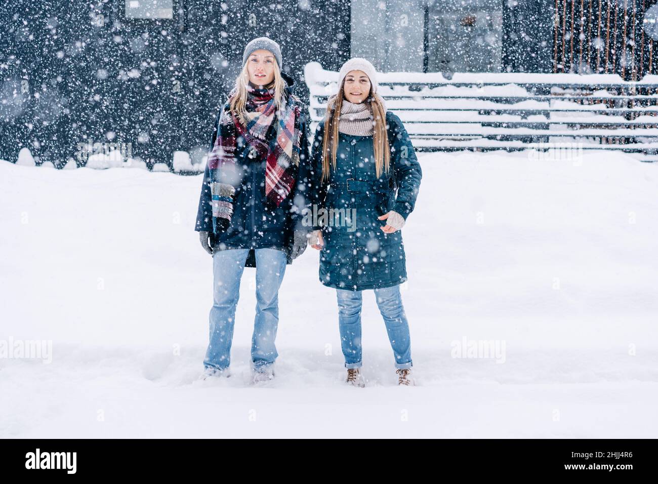 Two young women in warm winter clothes stand under the snowfall Stock ...