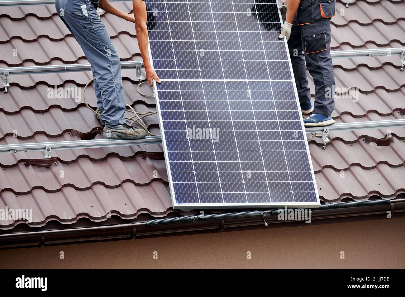 Men mounters lifting up photovoltaic solar moduls on roof of house ...