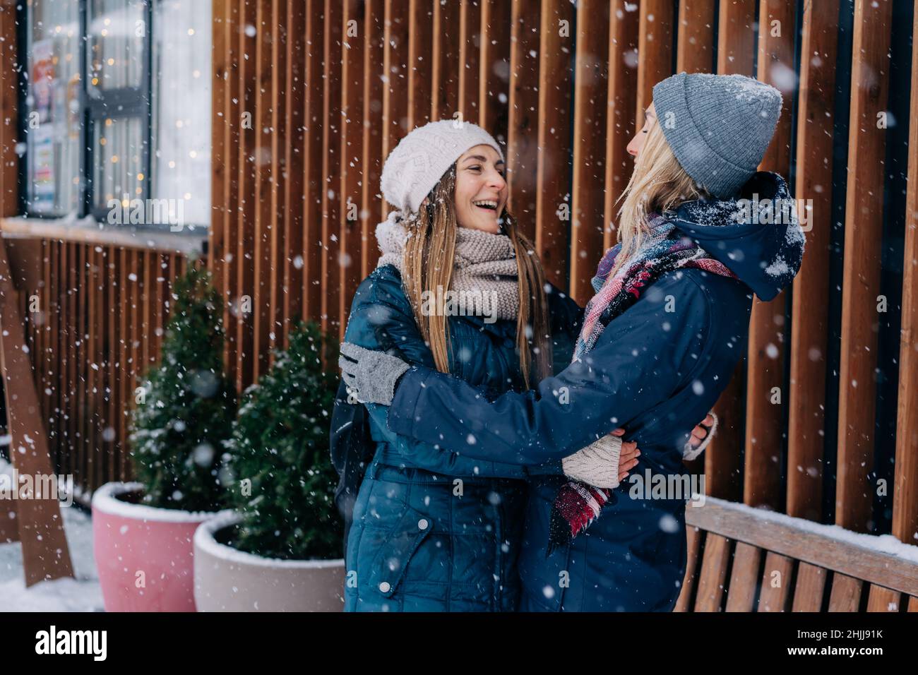 Adult female friends embracing and laughing rejoicing at the snowy cold ...
