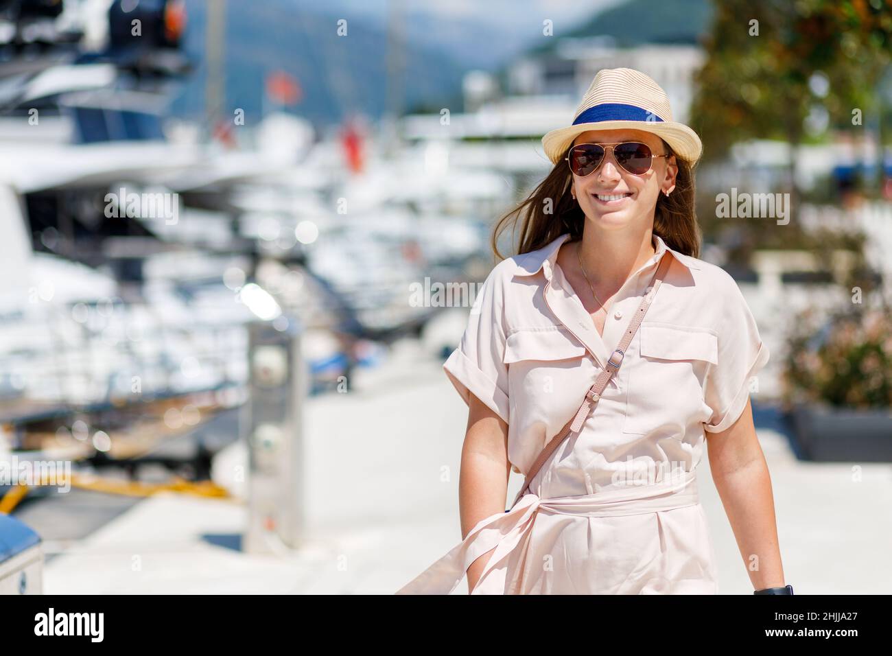Portrait of young lady in dress and hat walking near the marina pier ...