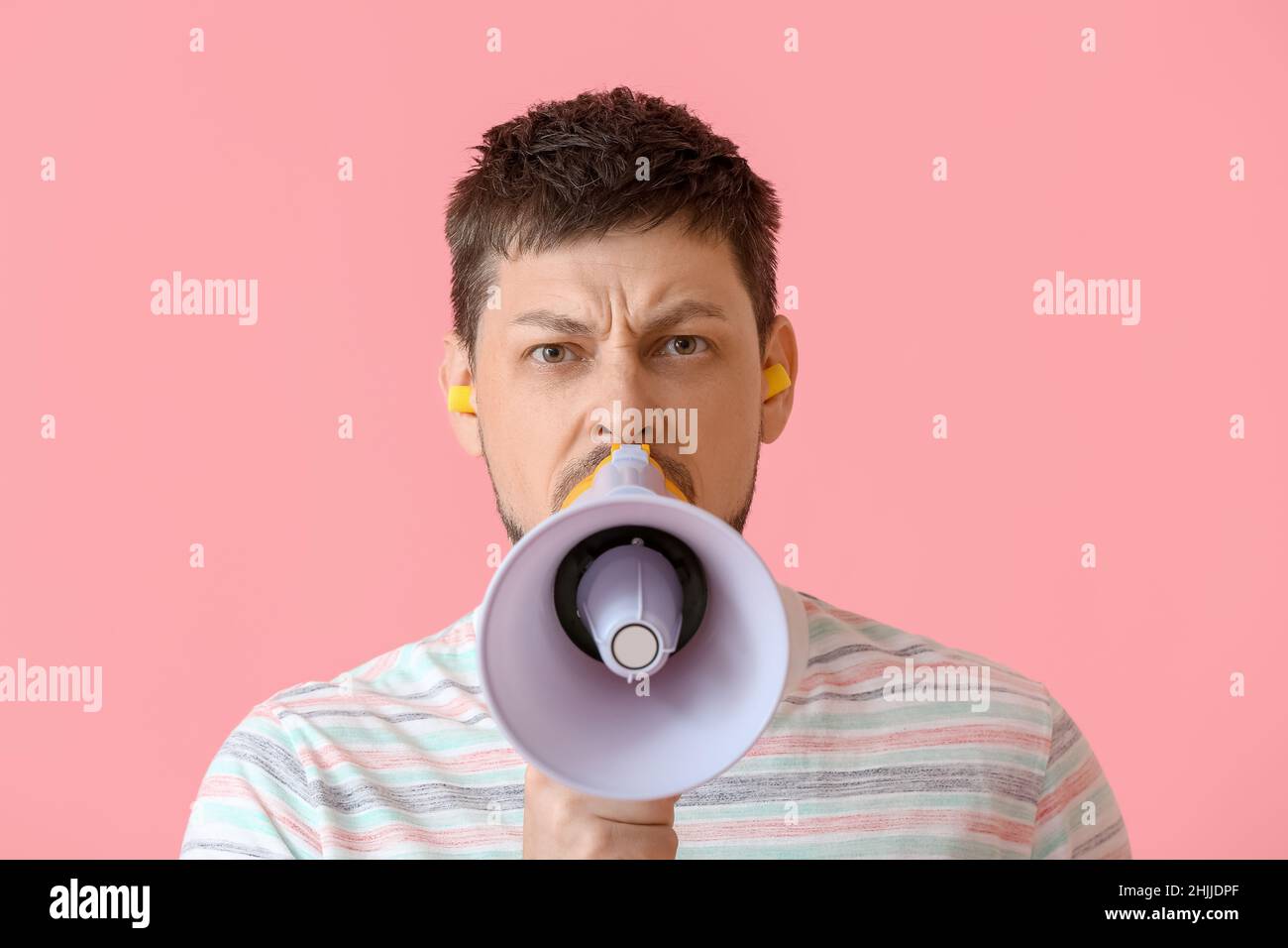 Angry young man with ear plugs shouting into megaphone on pink ...