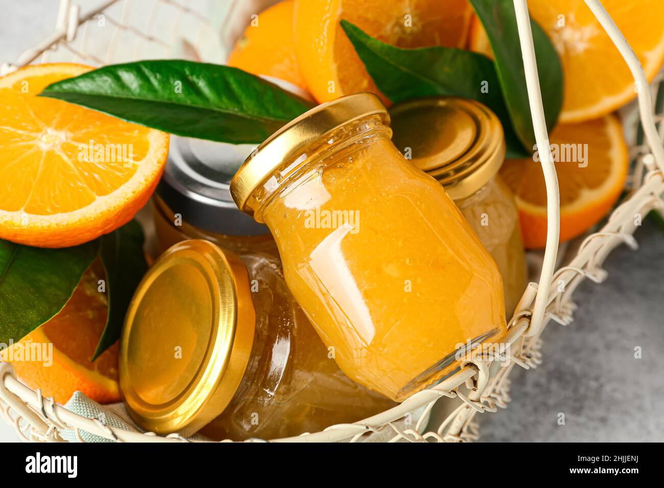 Basket with tasty orange jam in jars and leaves on table, closeup Stock ...