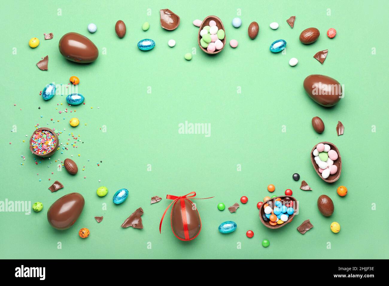 Frame made of chocolate Easter eggs, candies and sprinkles on green ...
