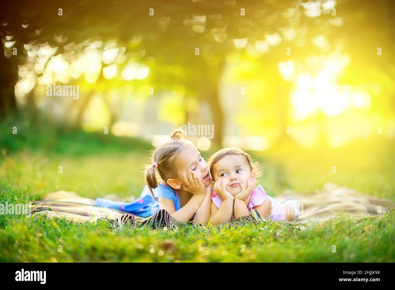 Cute children play in the park at sunset. Girls are lying on the grass ...