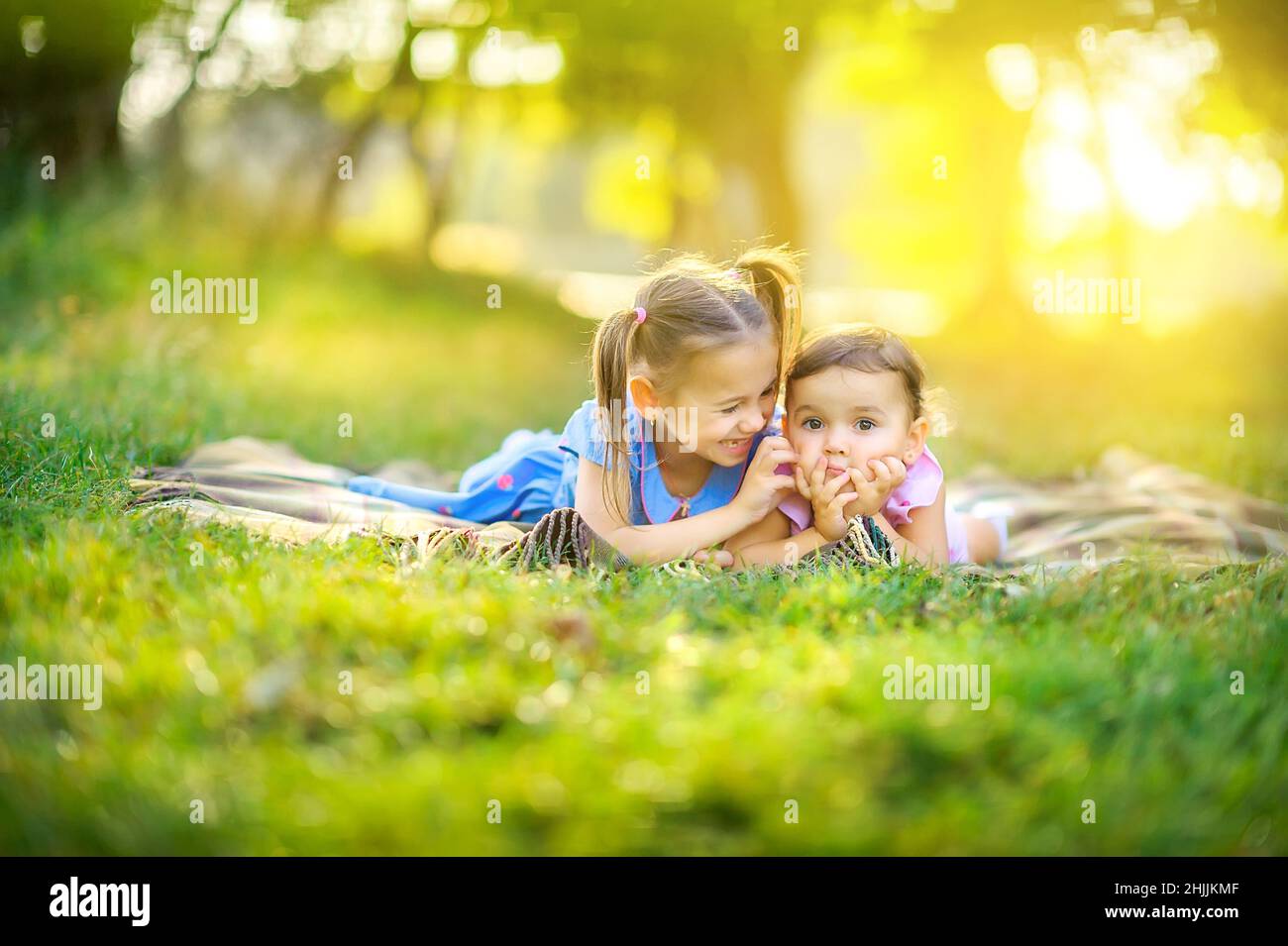 Cute children play in the park at sunset. Girls are lying on the grass ...