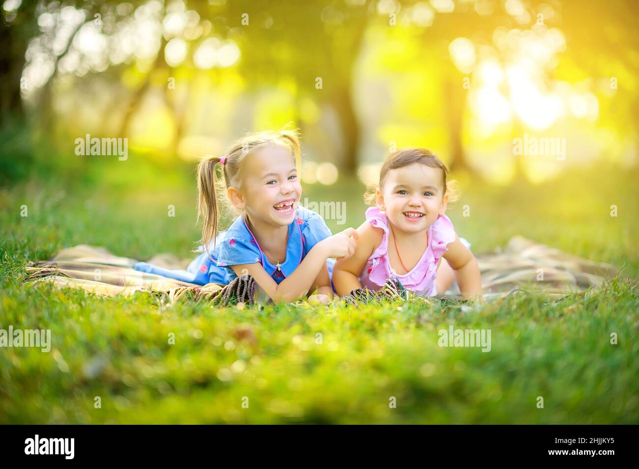 Cute children play in the park at sunset. Girls are lying on the grass ...