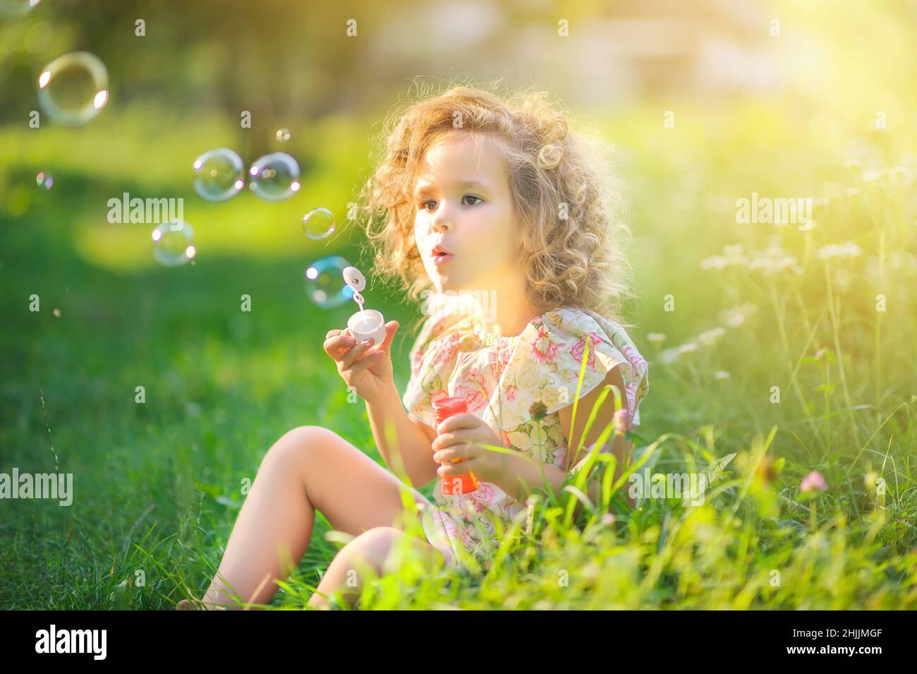 Cute girl blows soap bubbles while sitting on the grass in the park at ...