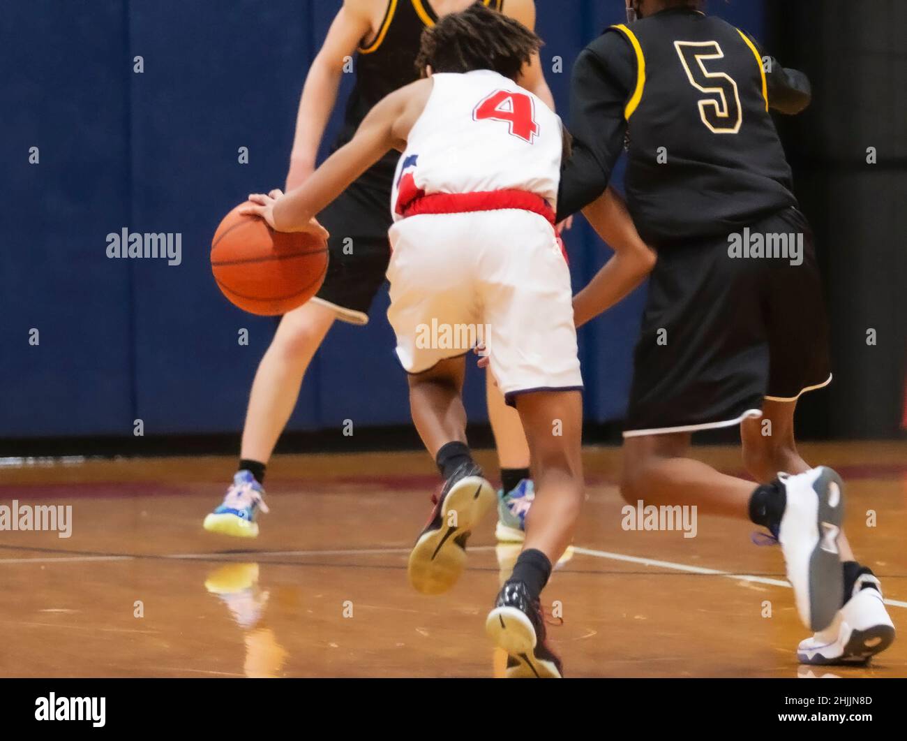 Rear view of a high school basketball player dribbling the ball toward ...