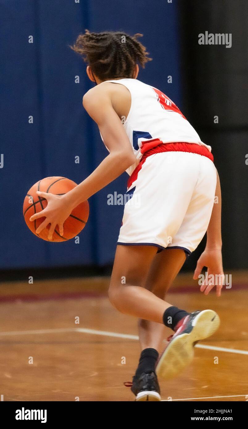 Rear view of a high school basketball player dribbling the ball down ...