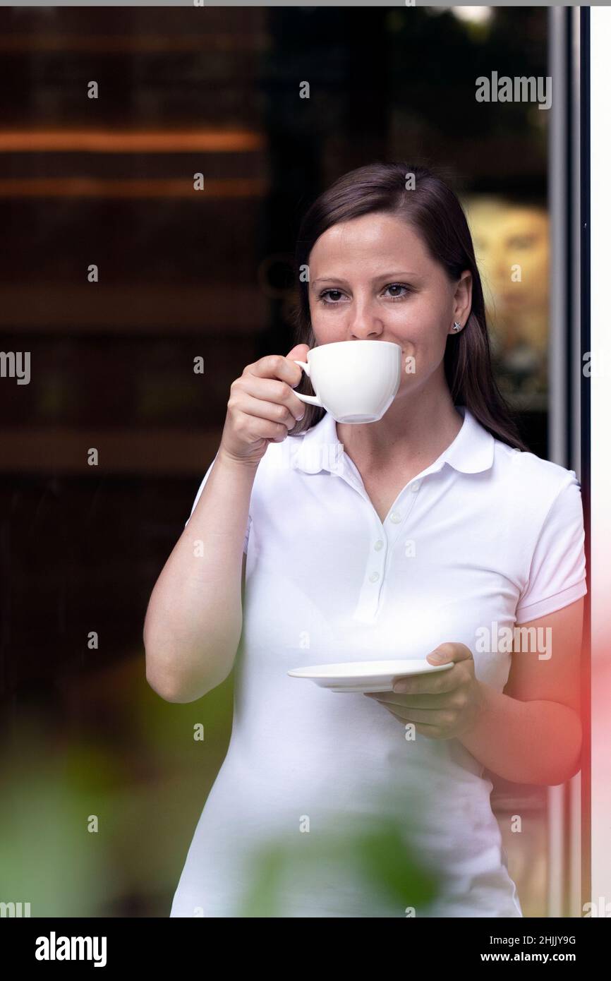 a young woman drinks coffee standing in the doorway of a cafe. coffee ...