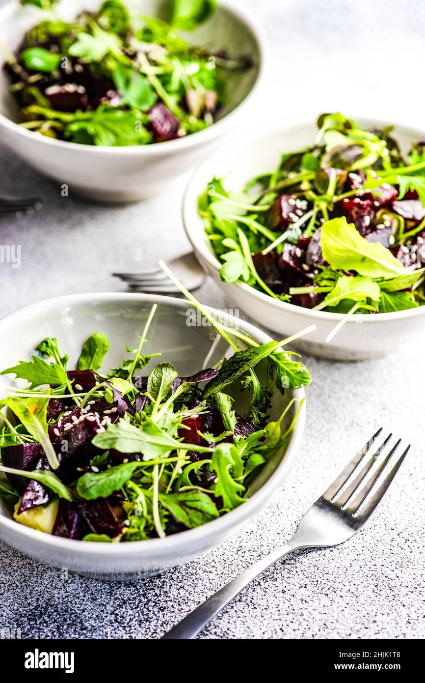 Three bowls of grilled beetroot with mixed leaf salad and sesame seeds ...