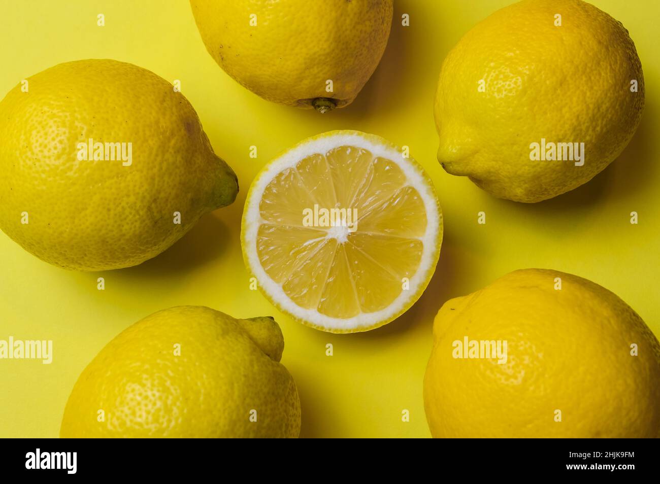 half cut lemon surrounded by five whole lemons on light yellow paper ...