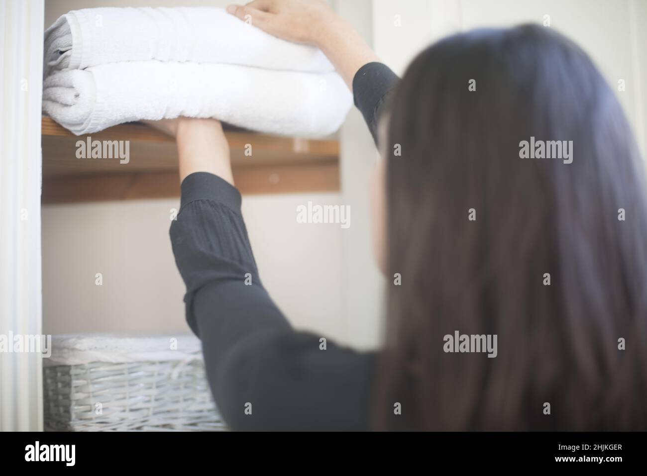 Back view of a female arranging folded towels on a shelf Stock Photo ...