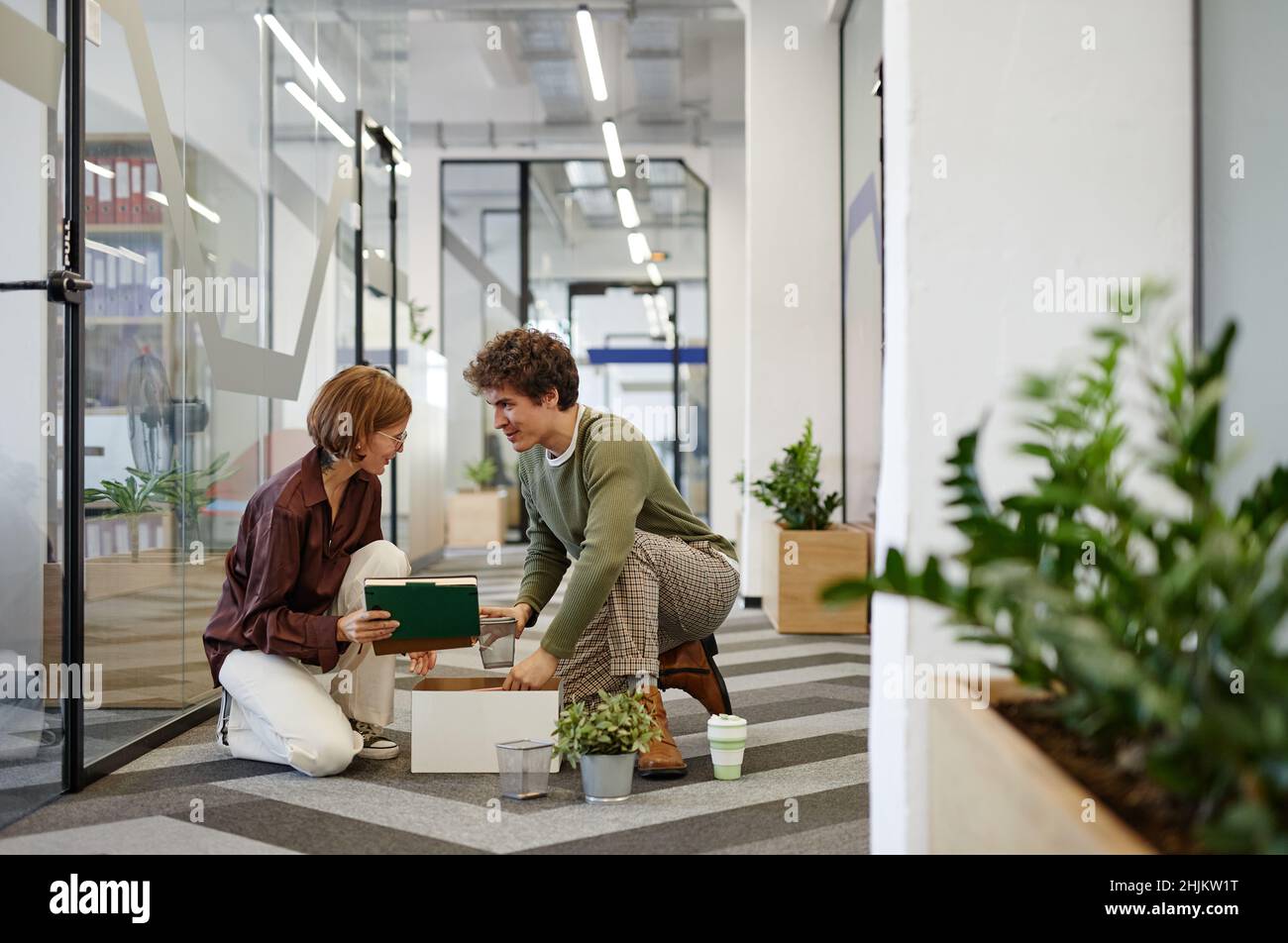 Full length portrait of friendly colleague helping young employee in ...