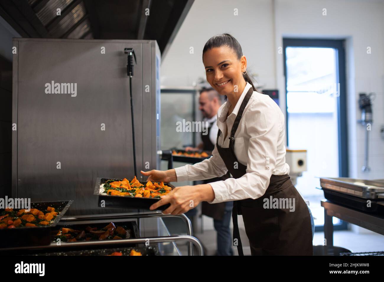 Happy female cook looking at camera and holding tray with baked pumpkin ...