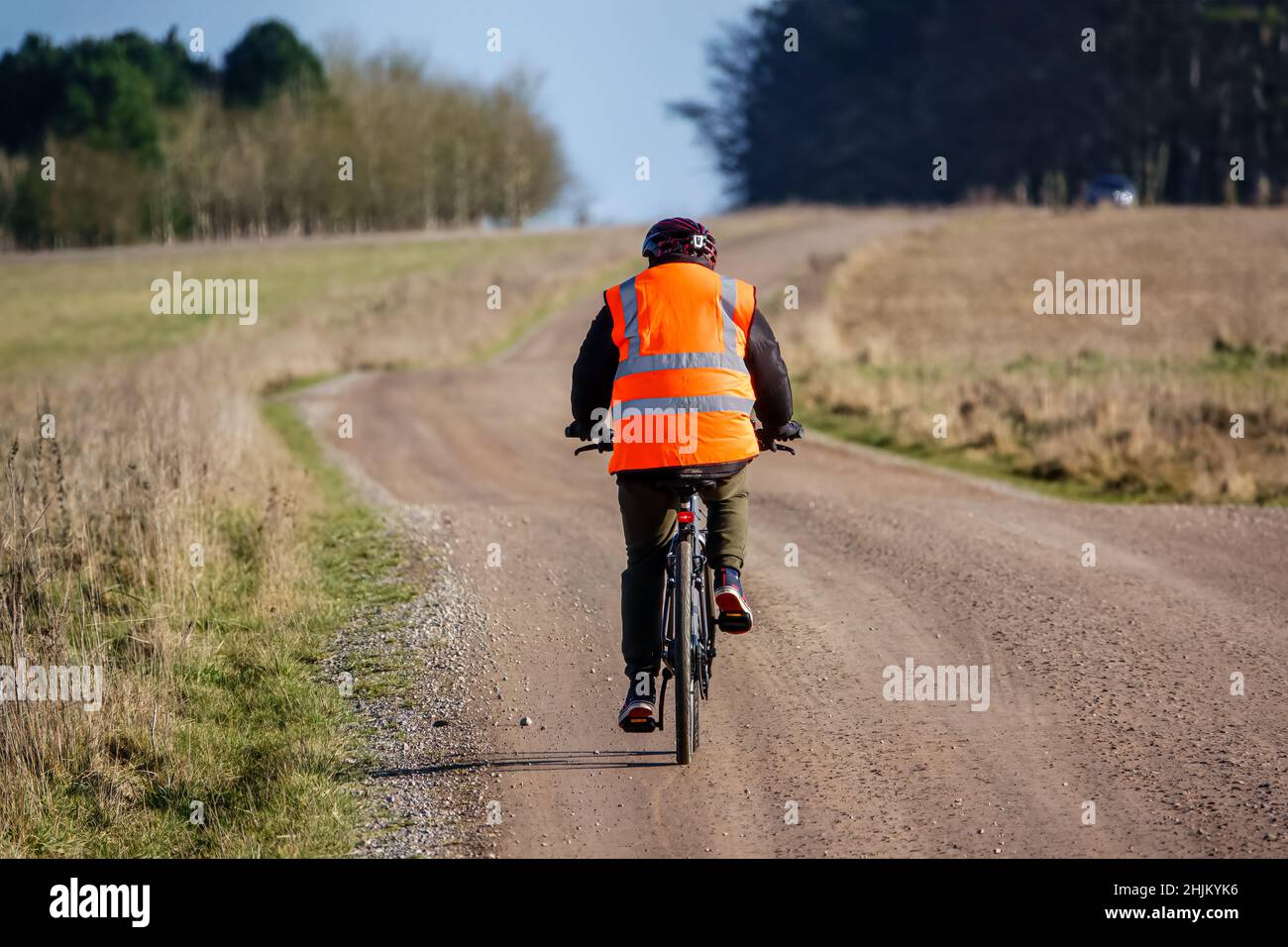 a casual cyclist in an orange high-vis jacket riding on a stone track ...