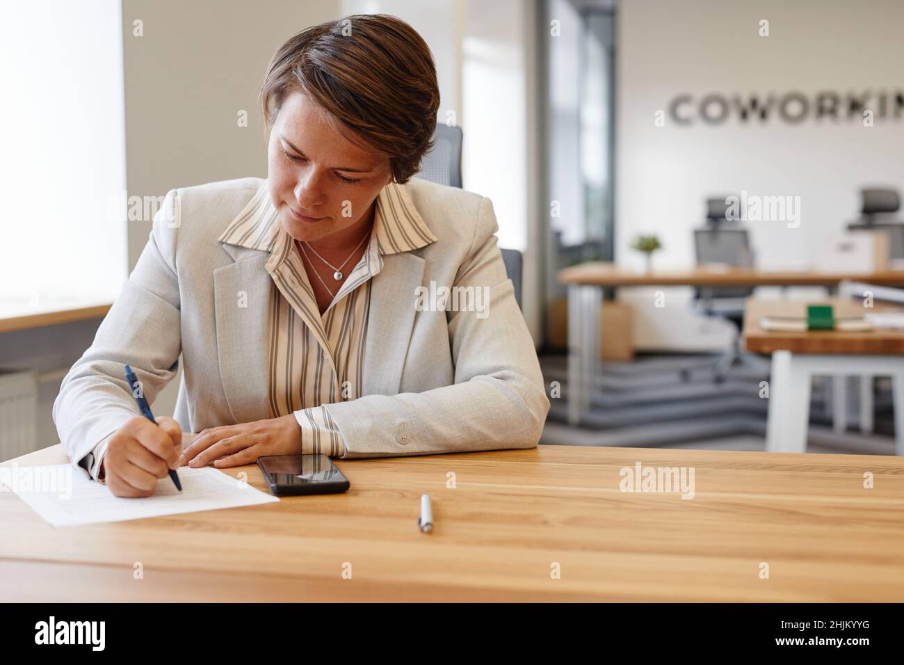 Portrait of adult female manager signing documents while sitting at ...