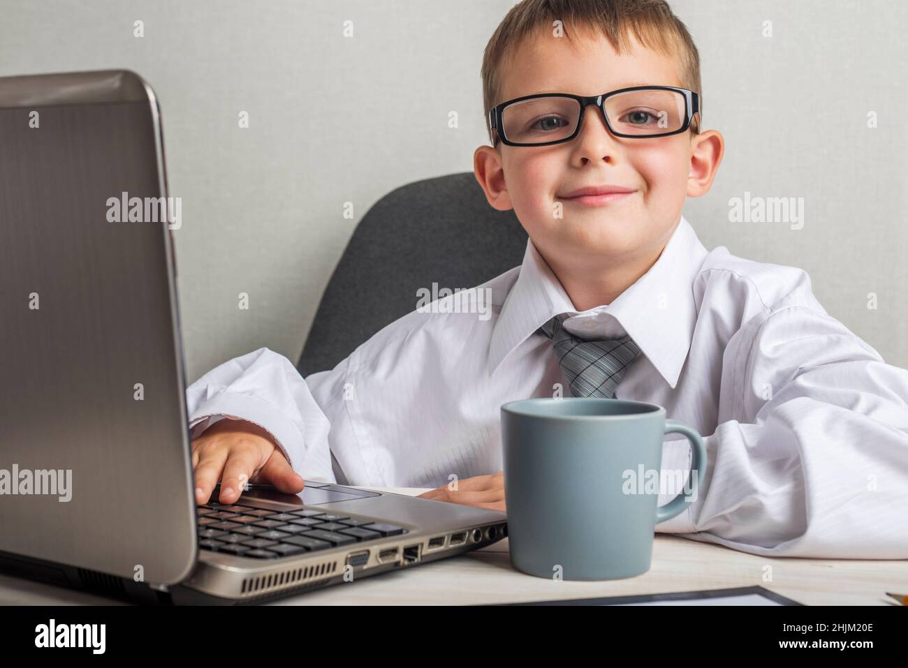 An adorable child is working on a laptop in suit and glasses. Little ...