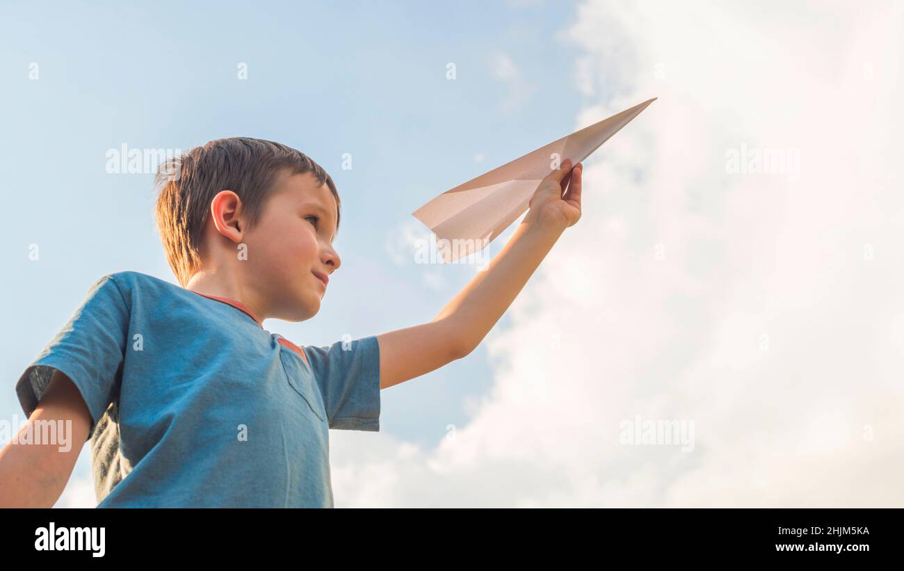 Happy child playing with paper airplane against the sky. A boy with ...