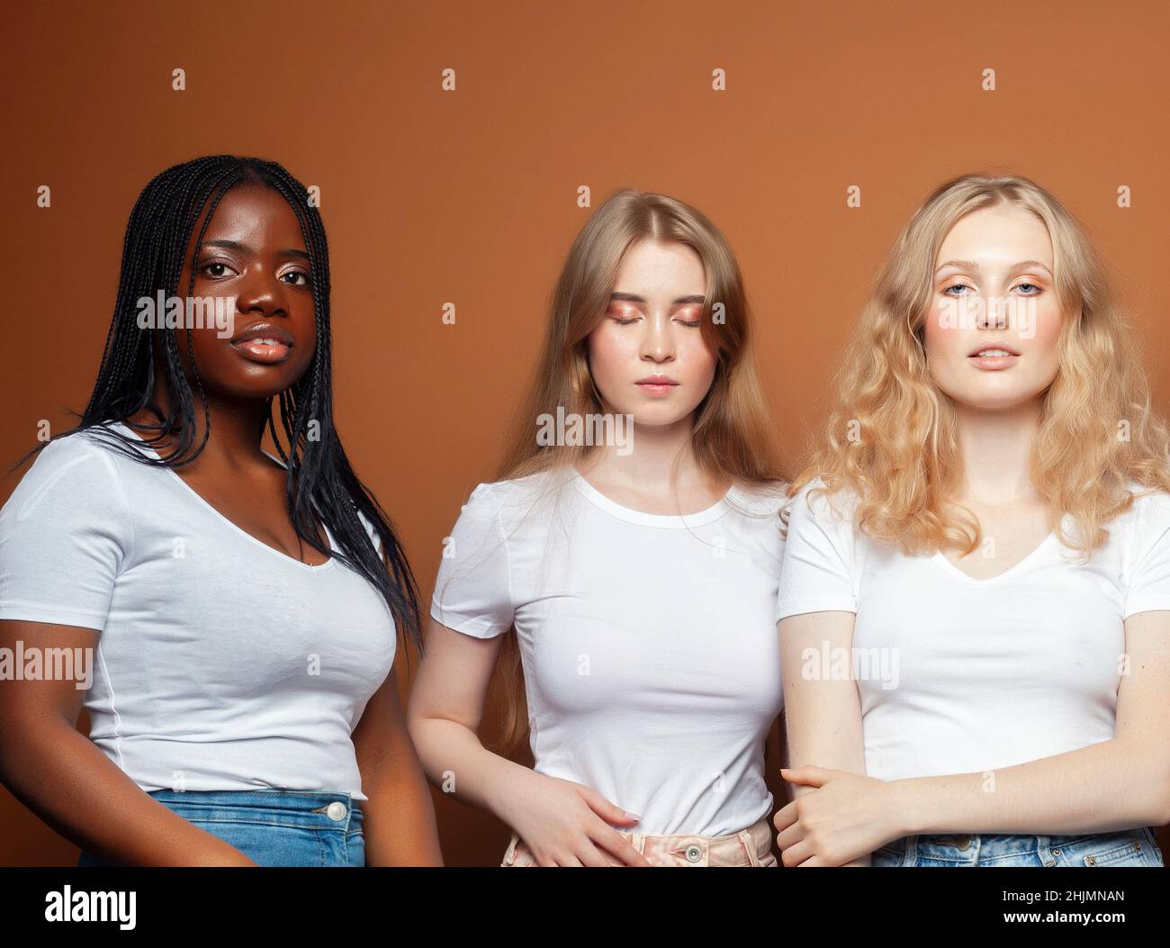 young pretty african and caucasian women posing cheerful together on brown background, lifestyle ...