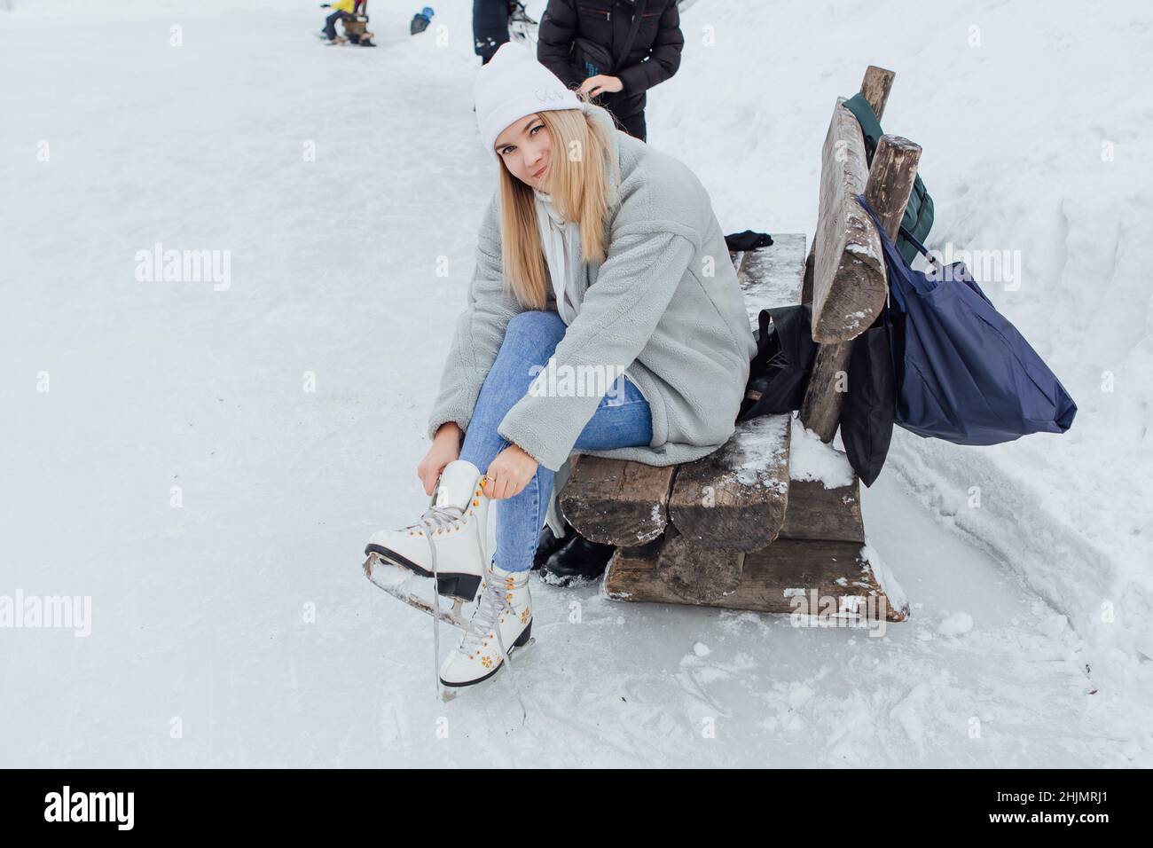 Lovely young woman sitting on the bench and puting on figure skates on ...