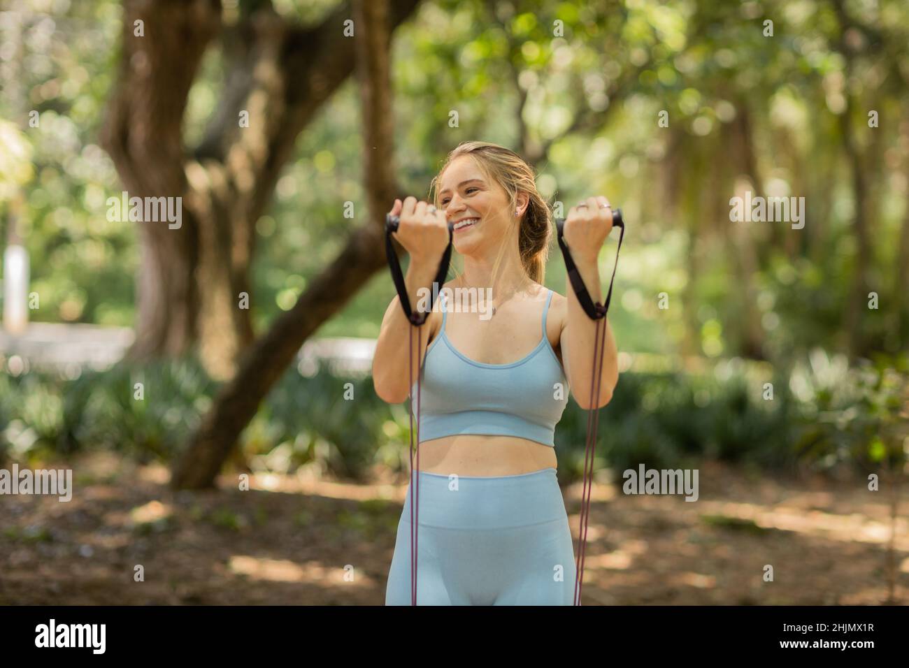 Strong woman working out with elastic rubber bands at a park outdoors ...