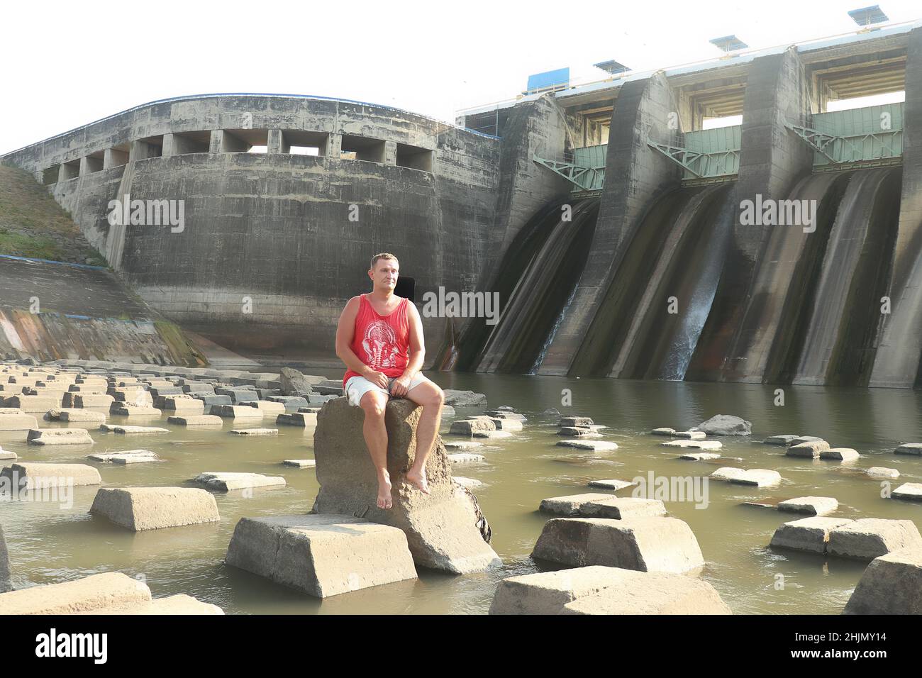 A man sits on concrete blocks under a dam. Dam and Waterfall Bendungan ...