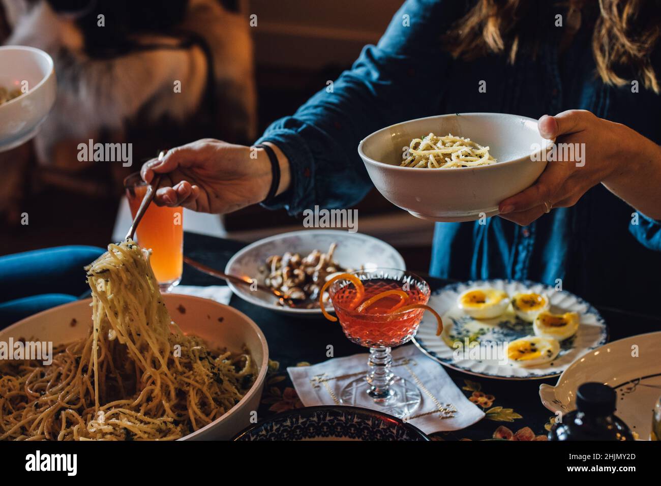 woman serving herself spaghetti noodles over table full of food, dinner ...