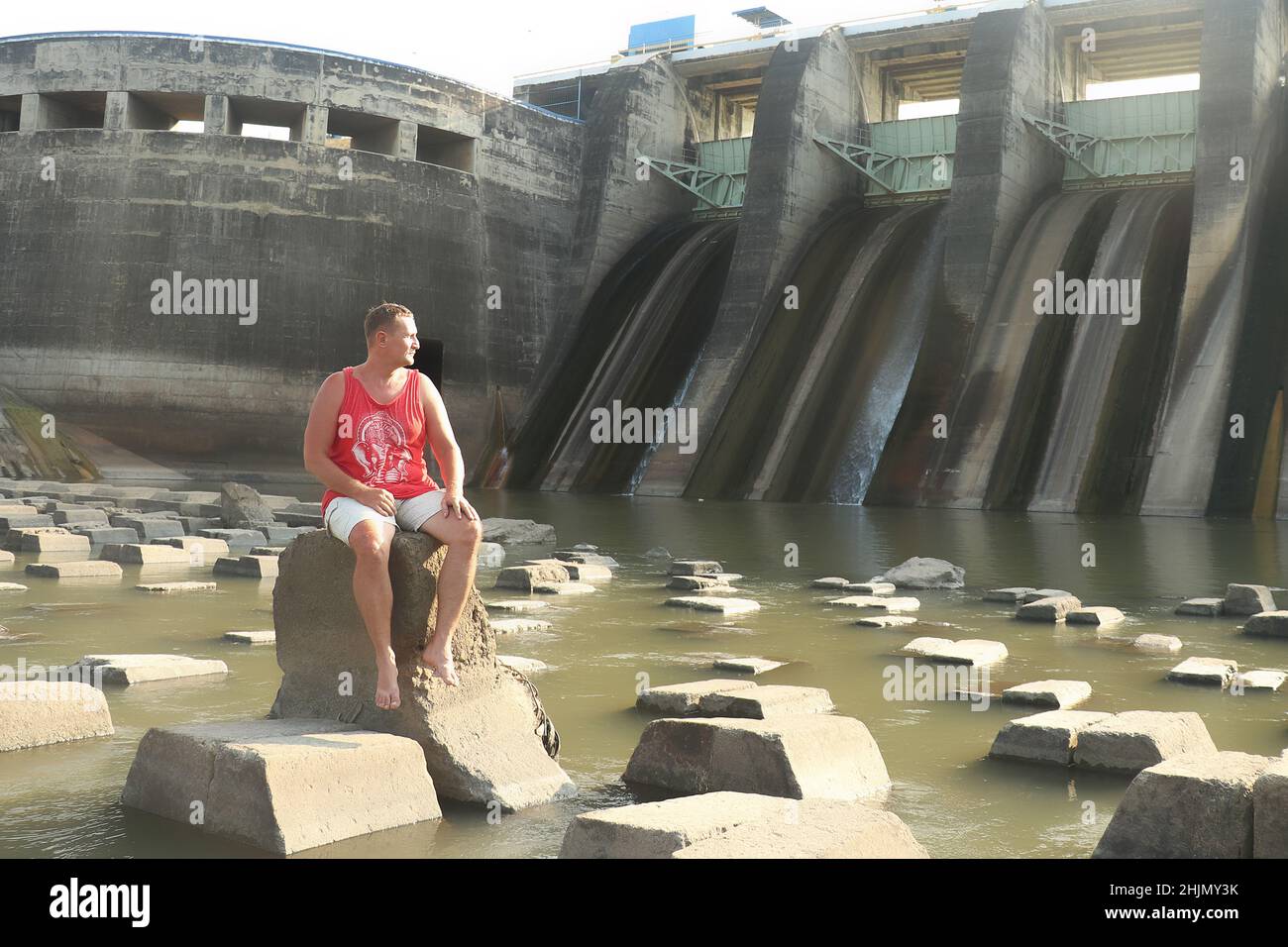 A man sits on concrete blocks under a dam. Dam and Waterfall Bendungan ...