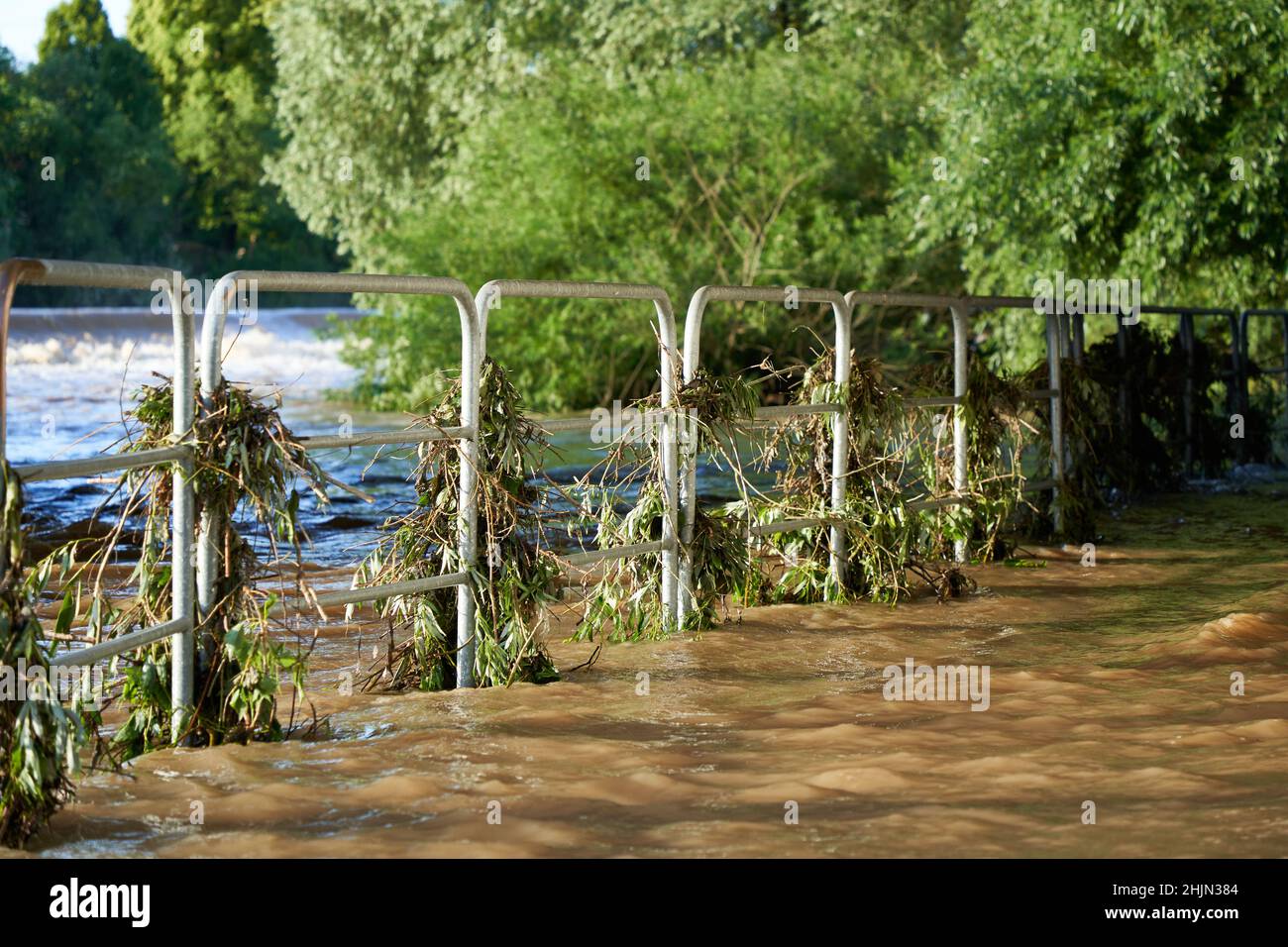 Flood on the river. Brown dirty water floods railings on the road. Weir ...