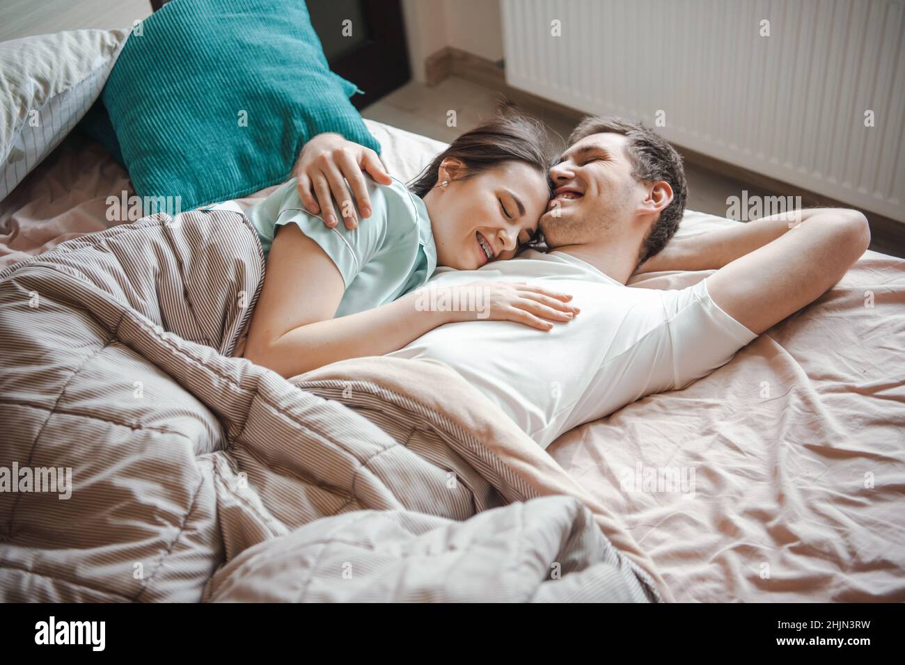 Caucasian couple spending the weekend time lying in bed and laughing ...