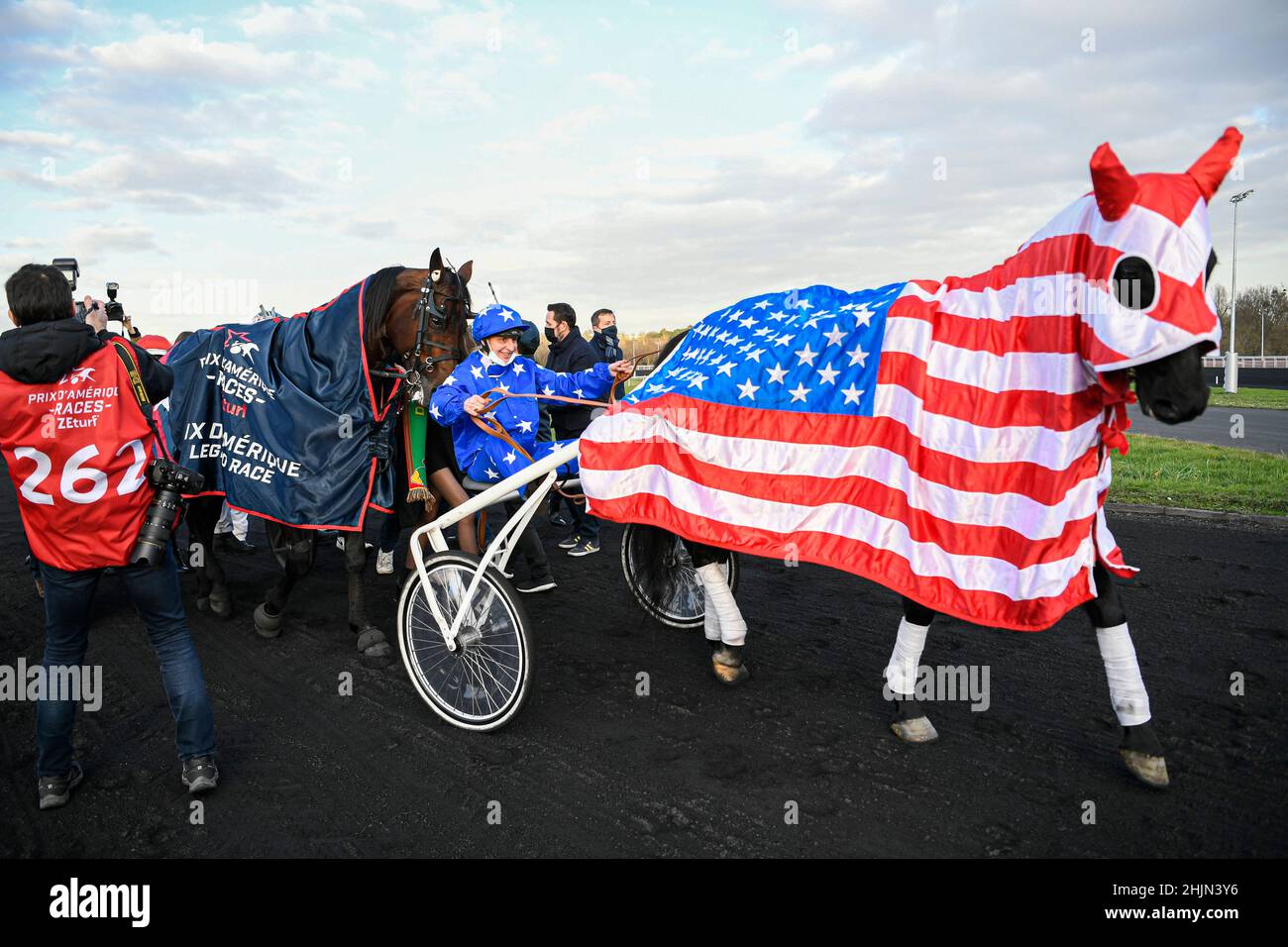 A jockey/driver parades with an American flag (USA) worn by the horse ...