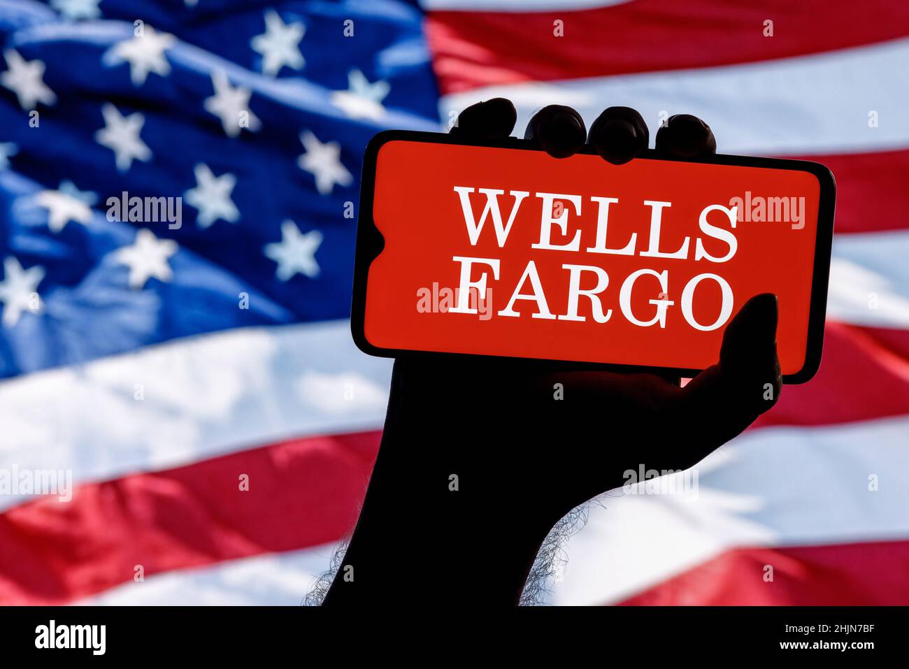Smartphone with Wells Fargo bank logo in clenched hand on background of ...