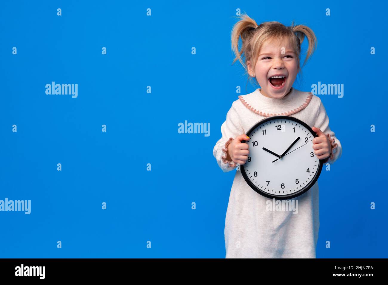 Beautiful teen girl holding wall clock over blue background Stock Photo ...