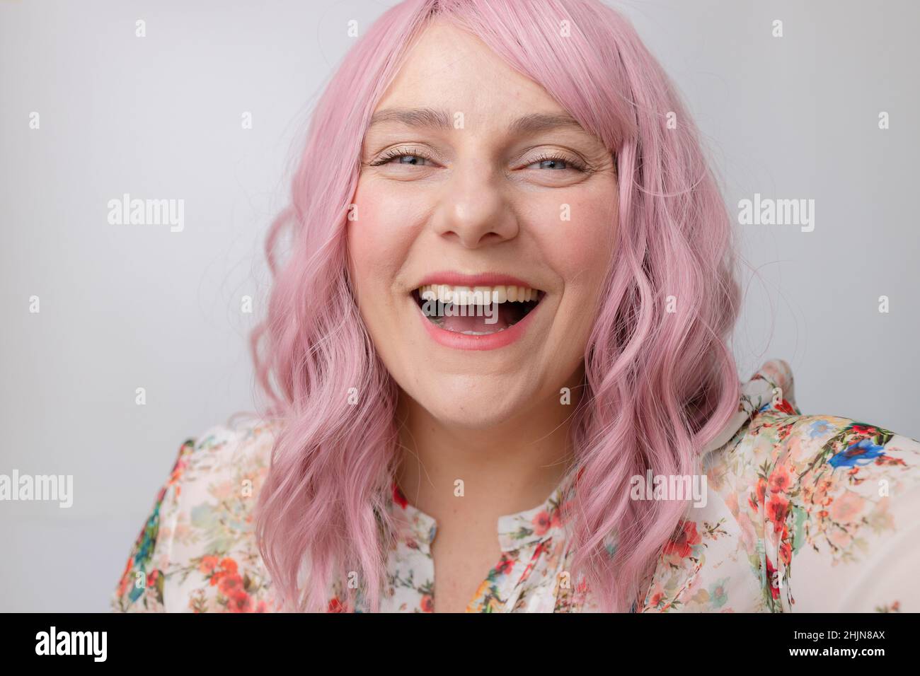 Portrait of young happy pink hair woman smiling on grey background ...