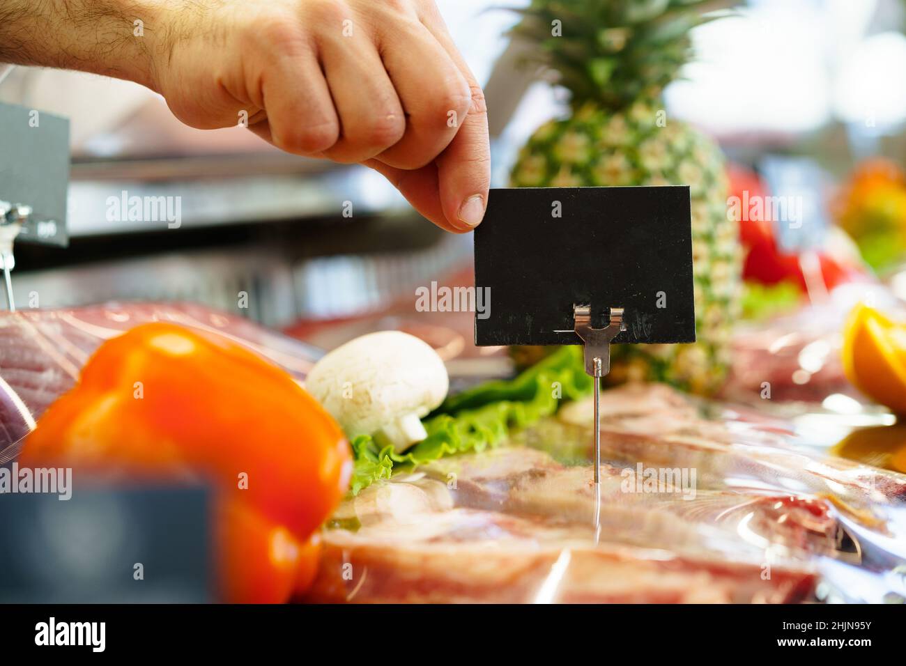 Male hand putting price tag on display of meat in shop, copy space ...