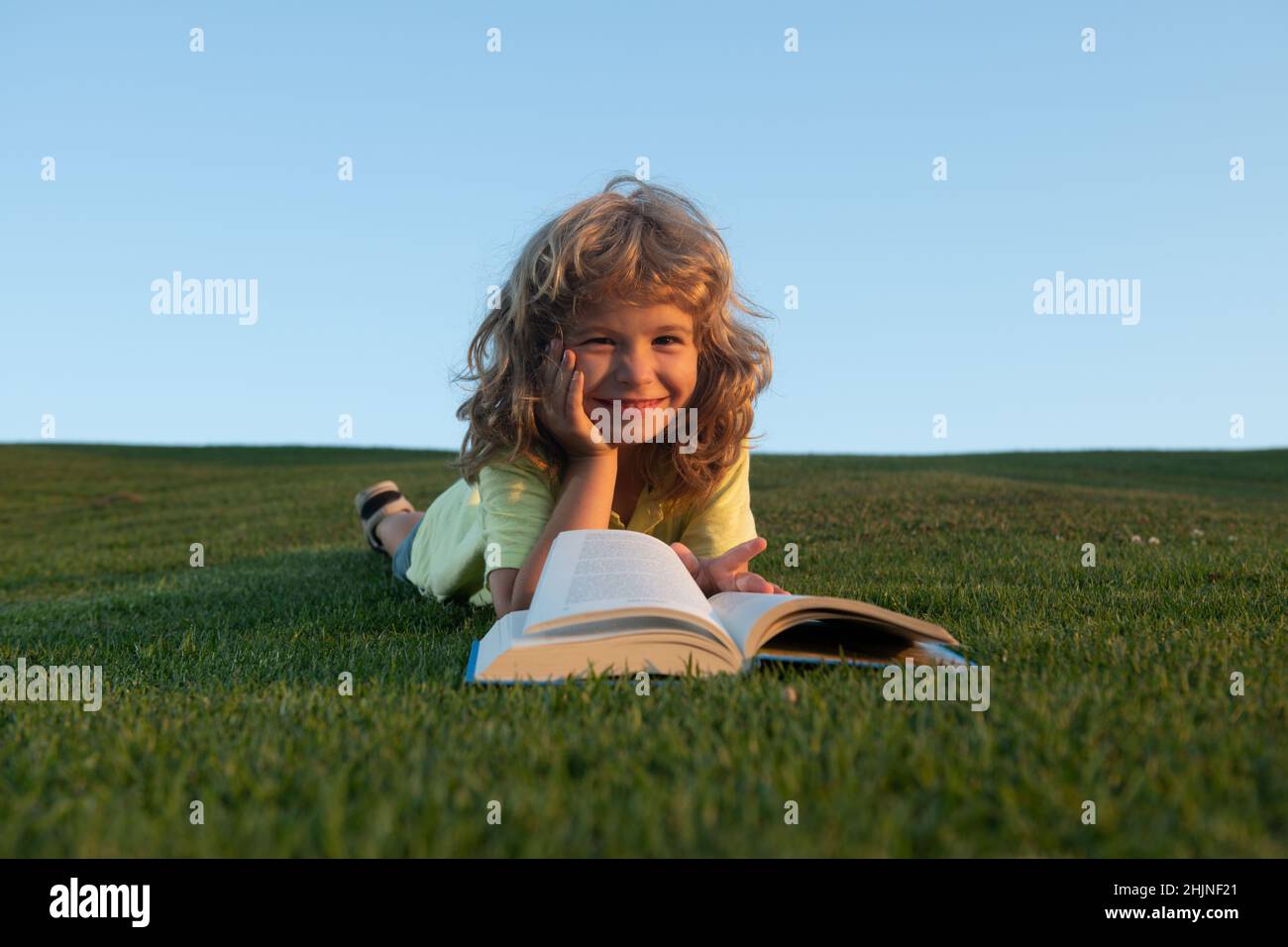 Smart kid boy reading book in park outdoor. Smiling funny child in t ...