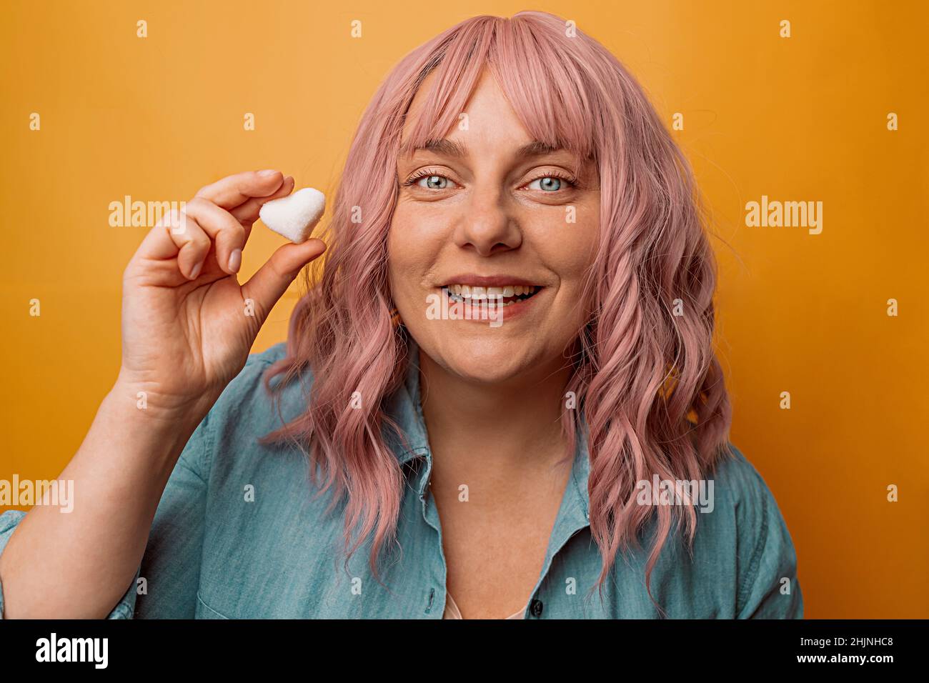 Happy woman holding white love shape jelly gummy in hand over yelow ...