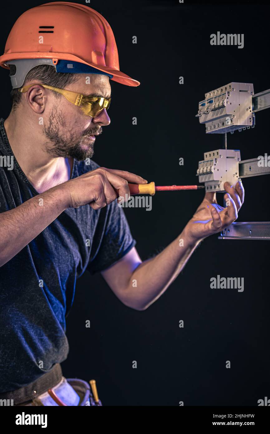 A male electrician works in a switchboard with an electrical connecting ...