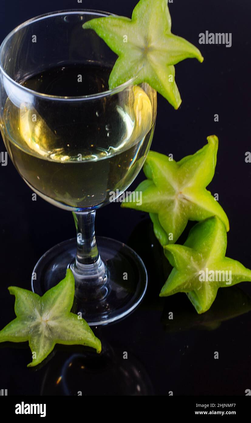fresh starfruit and a drink in a glass on a black background with water ...