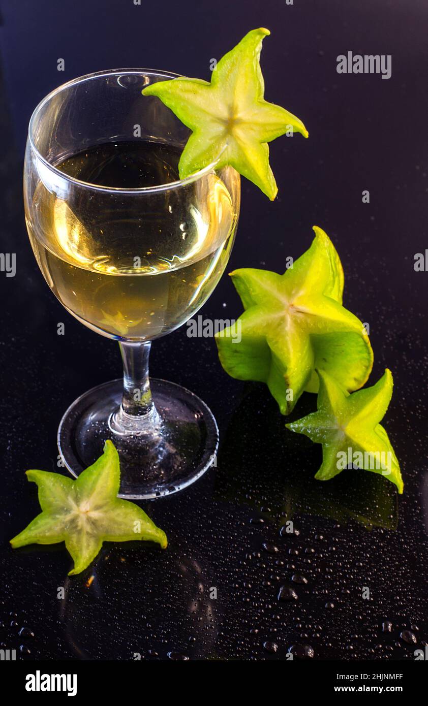 fresh starfruit and a drink in a glass on a black background with water ...