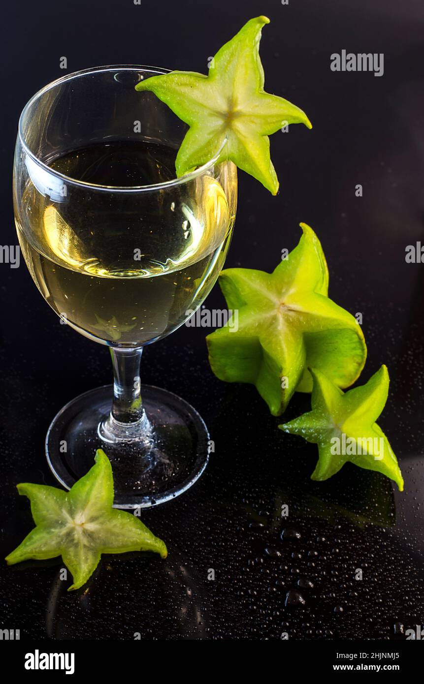 fresh starfruit and a drink in a glass on a black background with water ...