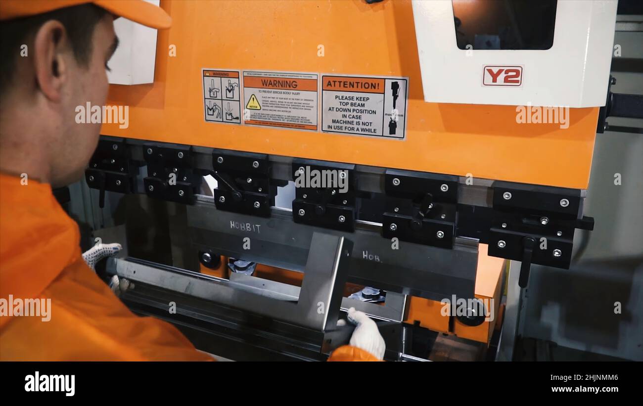 Worker in factory at metal skip machine putting work piece in. Clip ...