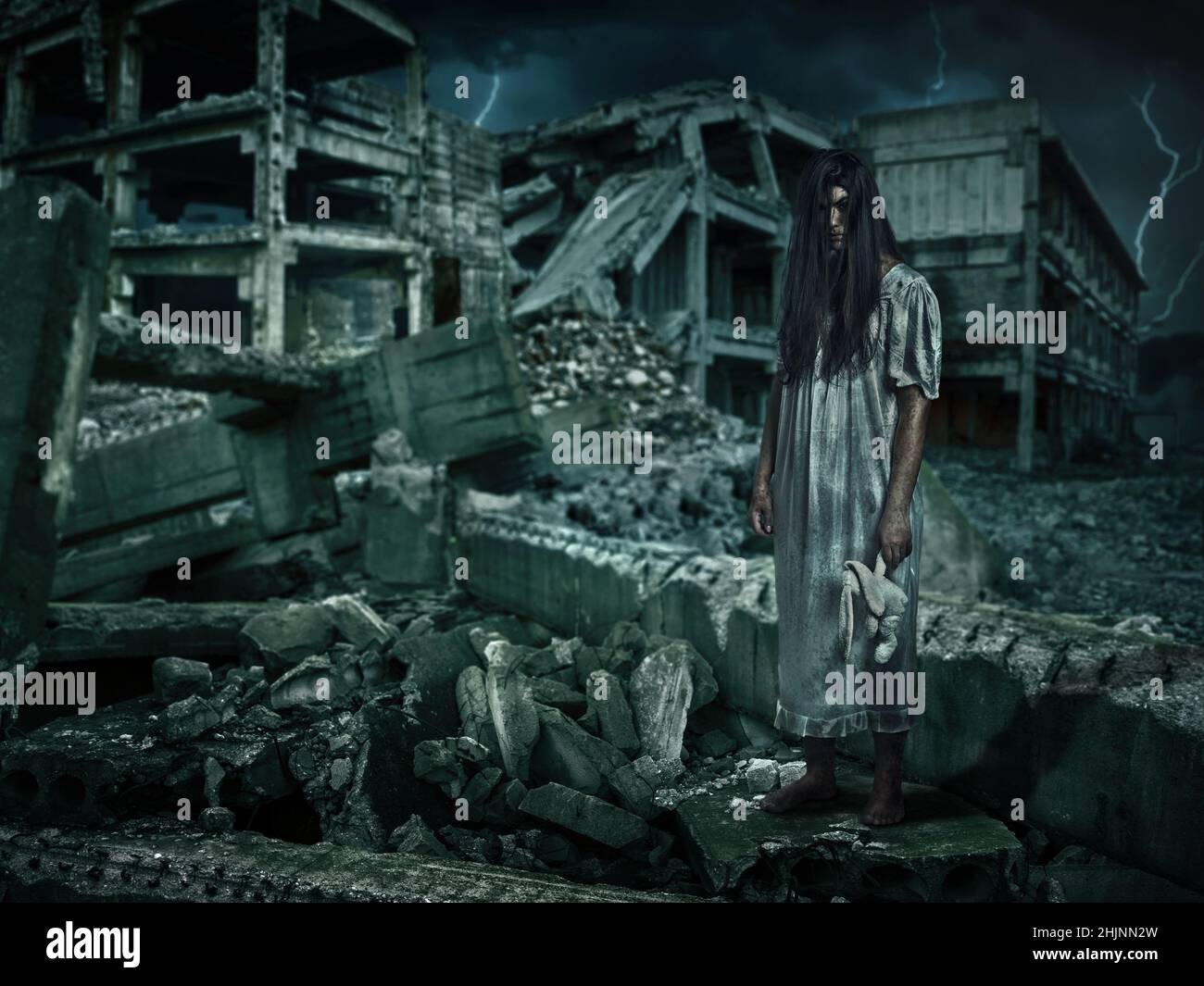 A sad homeless girl with a rabbit toy in the ruins of a war ravaged ...