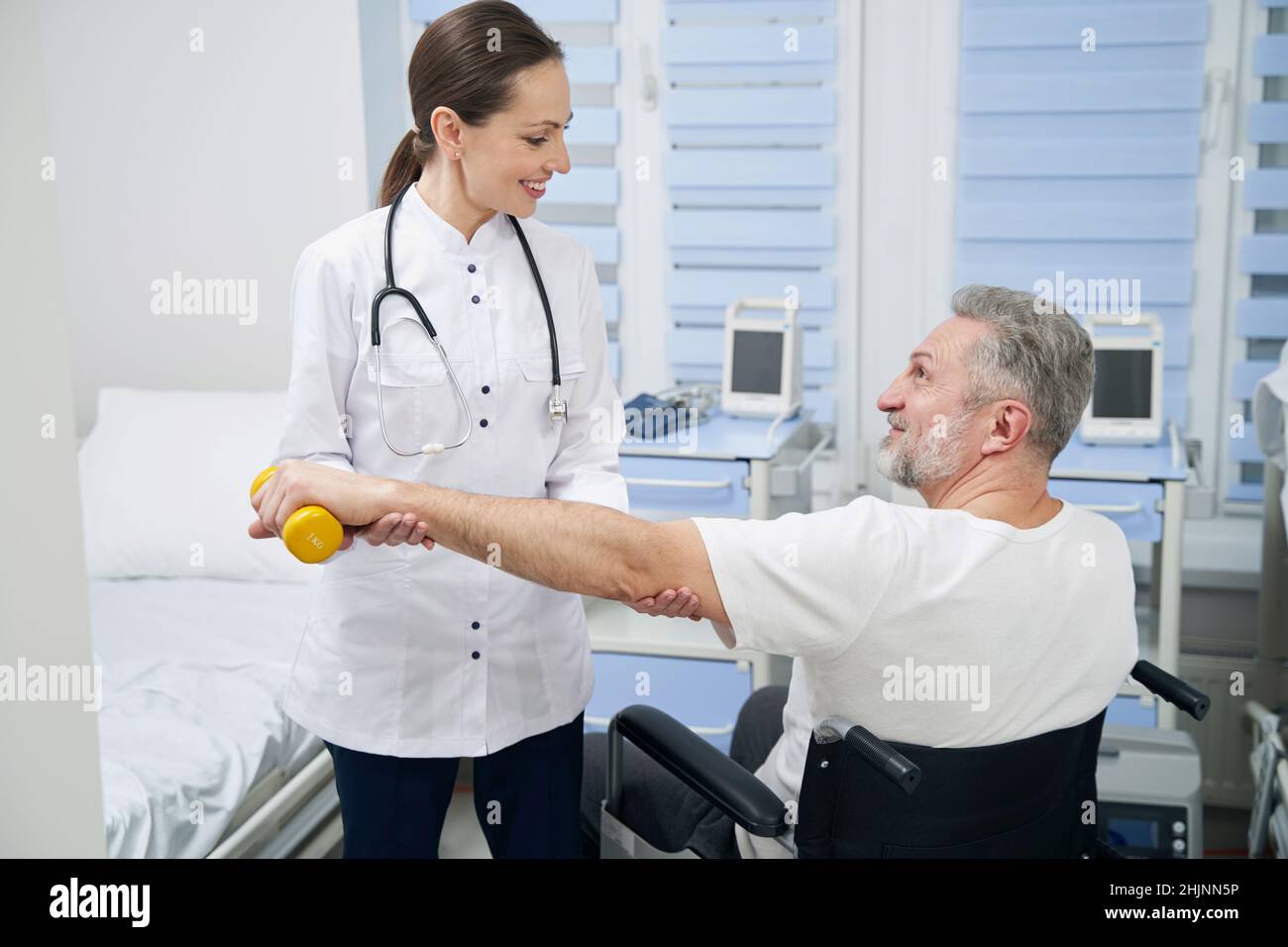 Male patient lifting hand weight assisted by friendly physiologist ...