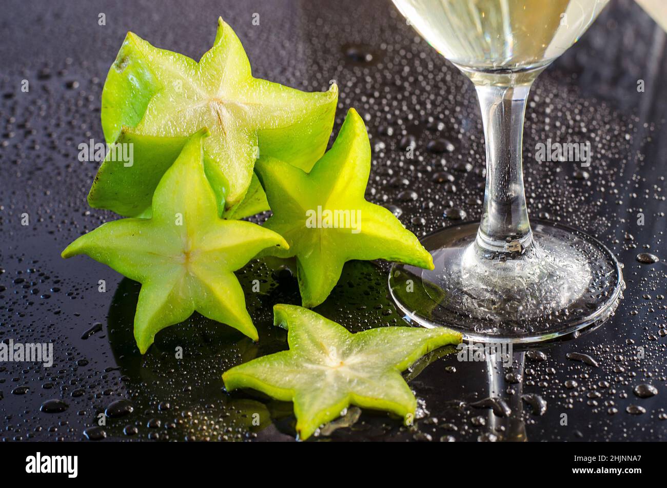 fresh starfruit and a drink in a glass on a black background with water ...